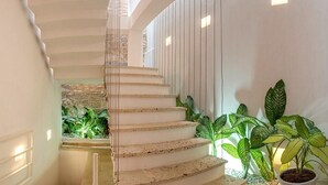 Escada em espiral com acabamento em pedra, rodeada por paredes brancas e plantas em vasos.