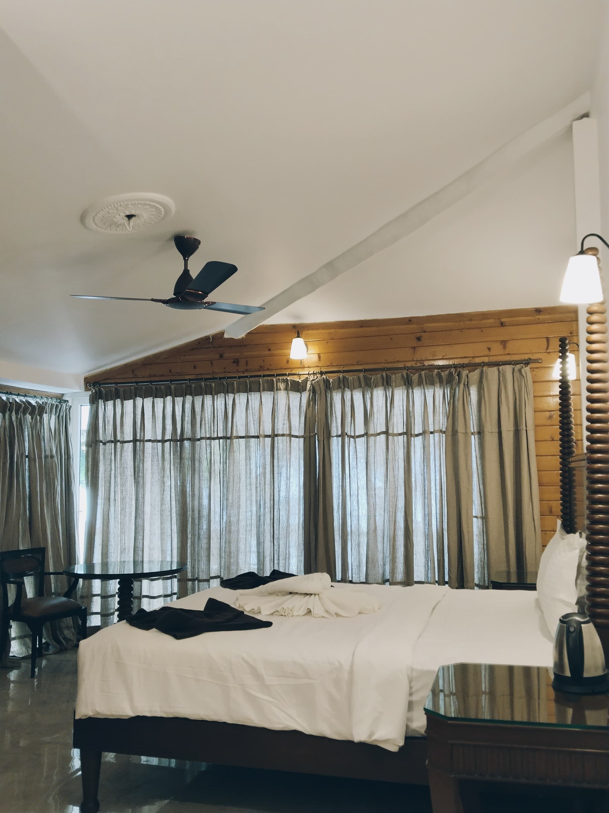 Quarto com cama, ventilador de teto, mesa e cortinas.