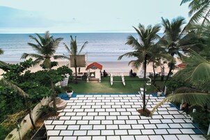 Vista da praia com palmeiras, área com azulejos brancos e uma pequena construção com telhado vermelho.