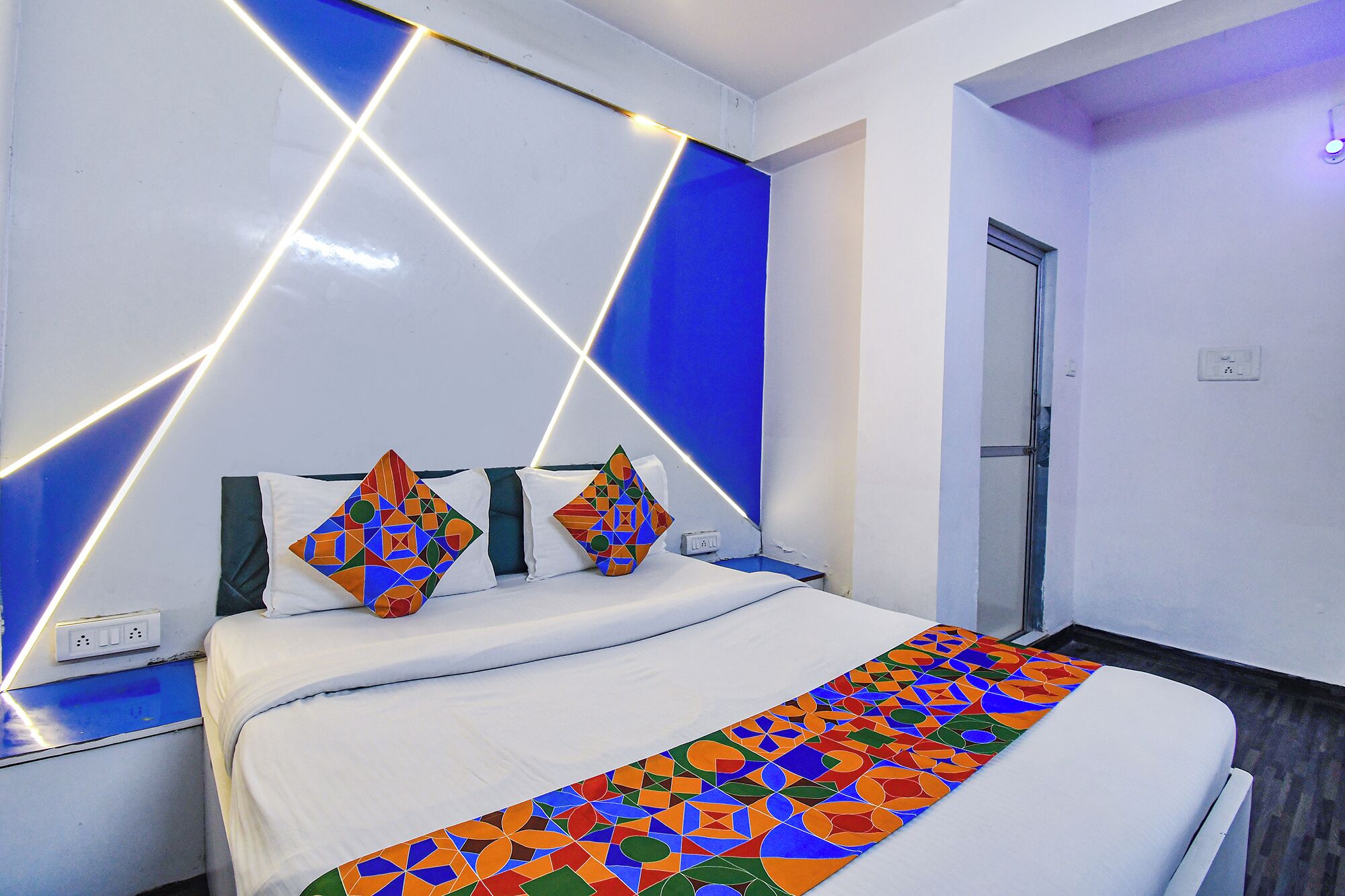 Quarto de hotel moderno com uma cama grande, almofadas com padrão geométrico e um cobertor colorido.