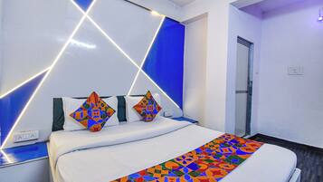 Quarto de hotel moderno com uma cama grande, almofadas com padrão geométrico e um cobertor colorido.