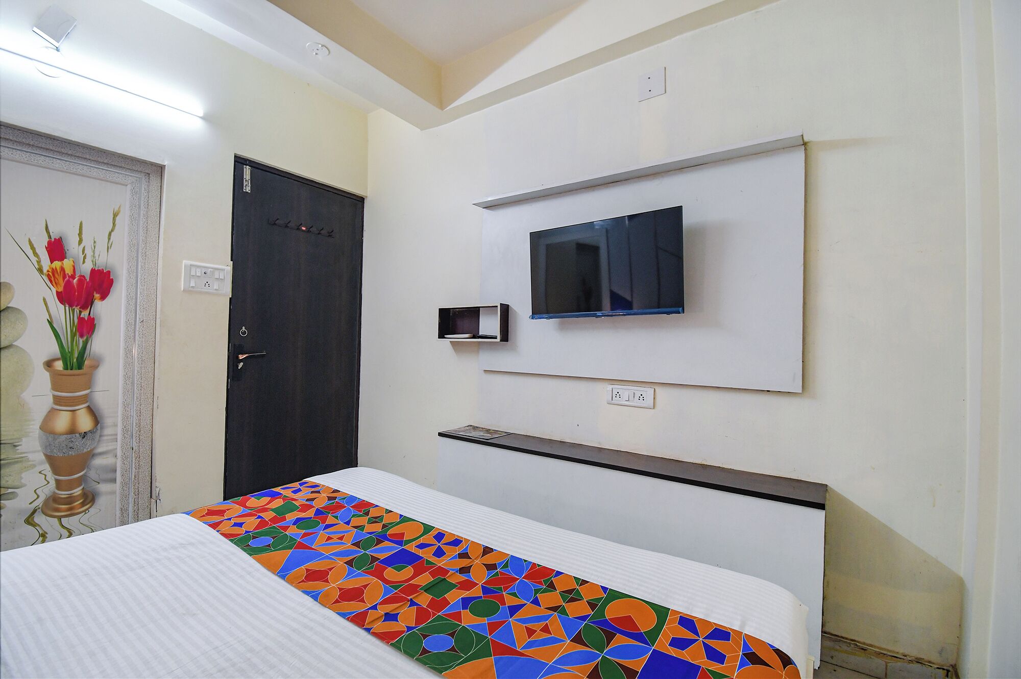 Quarto de hotel com cama, televisão na parede, porta e decoração na parede.