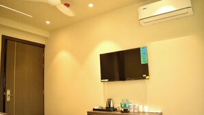 Quarto de hotel com uma cama, uma secretária com máquina de café, garrafas, copos e uma TV fixada na parede.
