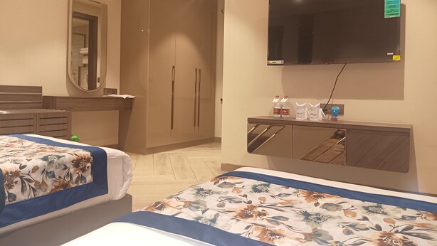 Quarto de hotel com duas camas, um guarda-roupa, um espelho, uma televisão e uma pequena mesa com produtos de higiene pessoal.