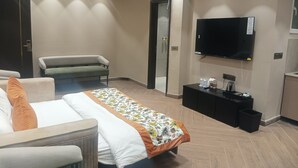 Quarto de hotel moderno com cama, sofá, banqueta, televisão e minibar.