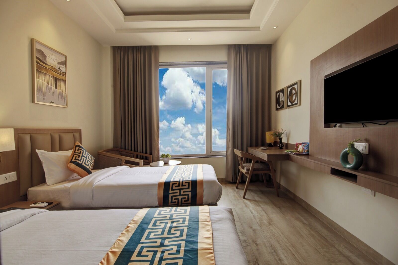 Quarto de hotel com duas camas, uma escrivaninha, televisão e janela com vista para o céu.