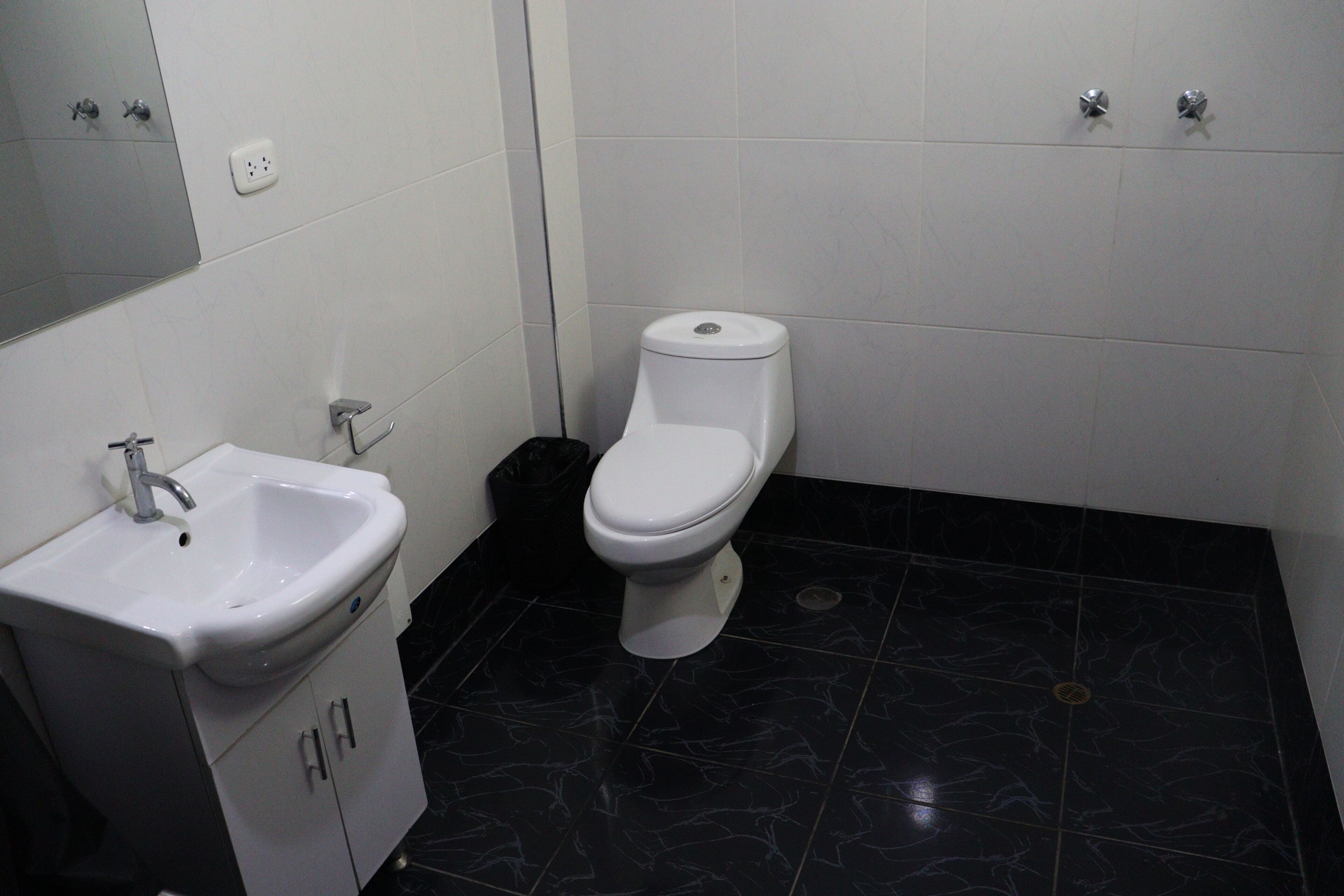 Casa de banho com lavatório branco, sanita e chão em mosaico preto.