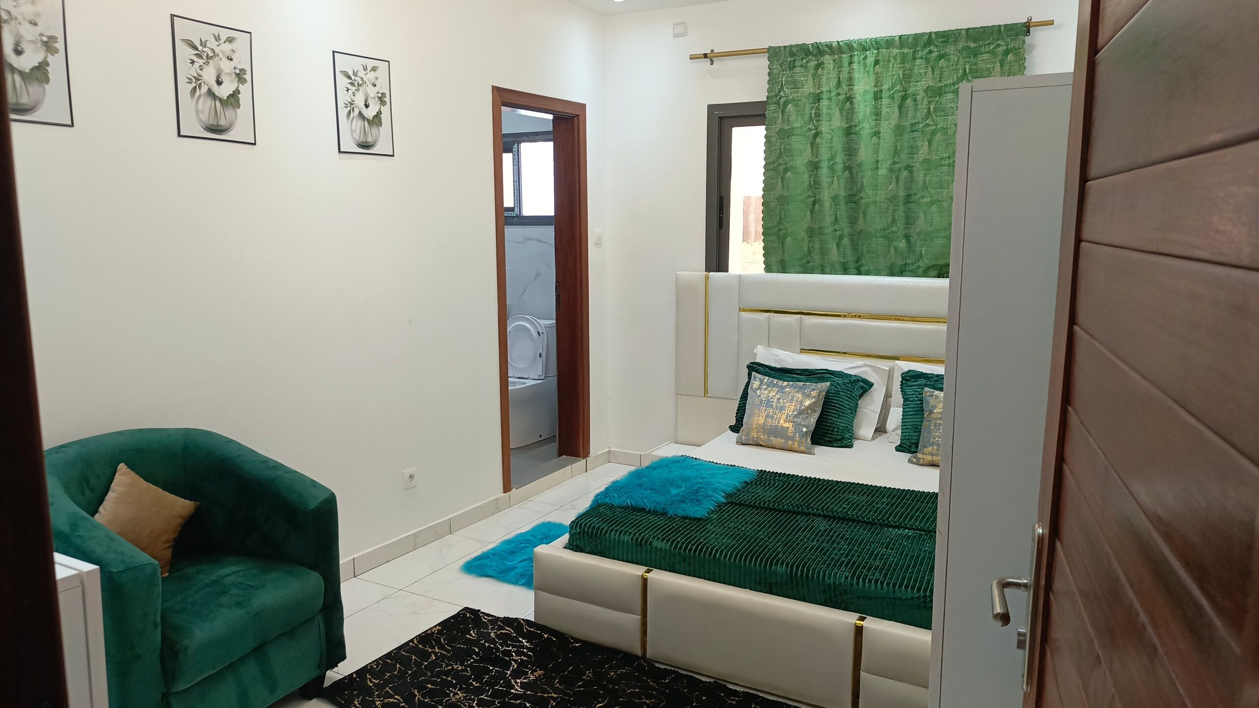 Quarto com cama, cortinas verdes, uma cadeira verde e um guarda-roupa branco.