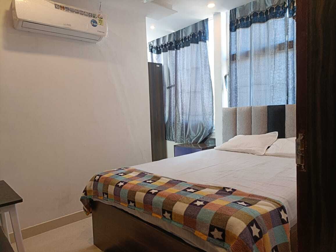 Quarto com cama, mesa de cabeceira, guarda-roupa e janela com cortinas.