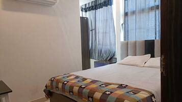 Quarto com cama, mesa de cabeceira, guarda-roupa e janela com cortinas.