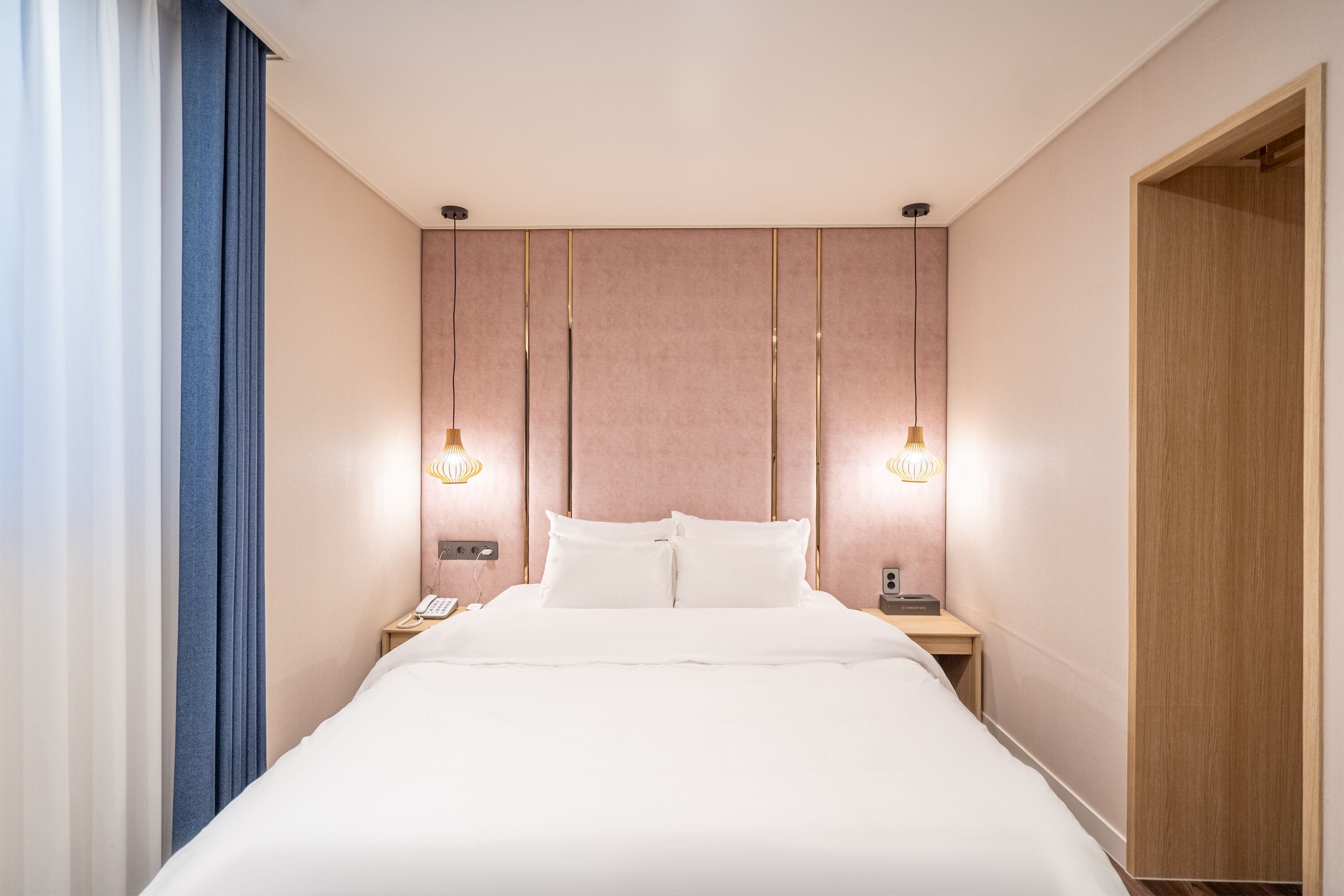 Quarto de hotel moderno com uma cama grande, duas mesas de cabeceira e um guarda-roupa de madeira.