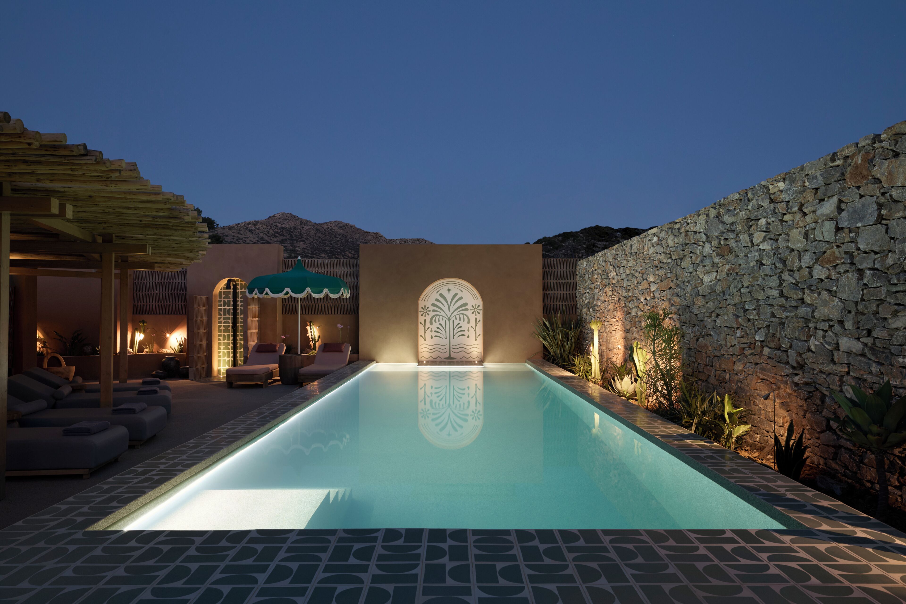 Piscina com parede de pedra e pérgula de um lado.