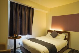 Quarto de hotel com uma cama bem arrumada, uma pequena mesa redonda com uma garrafa e copos, e uma janela grande com cortinas.