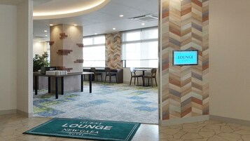 Um hall de hotel com parede em padrão losango, balcão de recepção e diversas áreas de estar.
