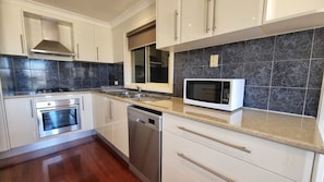 Uma cozinha moderna com armários brancos, fogão de aço inoxidável, lava-louças e micro-ondas.