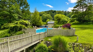 Um quintal com piscina, deck de madeira e vegetação exuberante.
