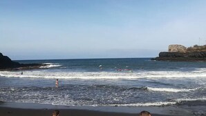 Uma praia com ondas, um penhasco rochoso e céu claro.