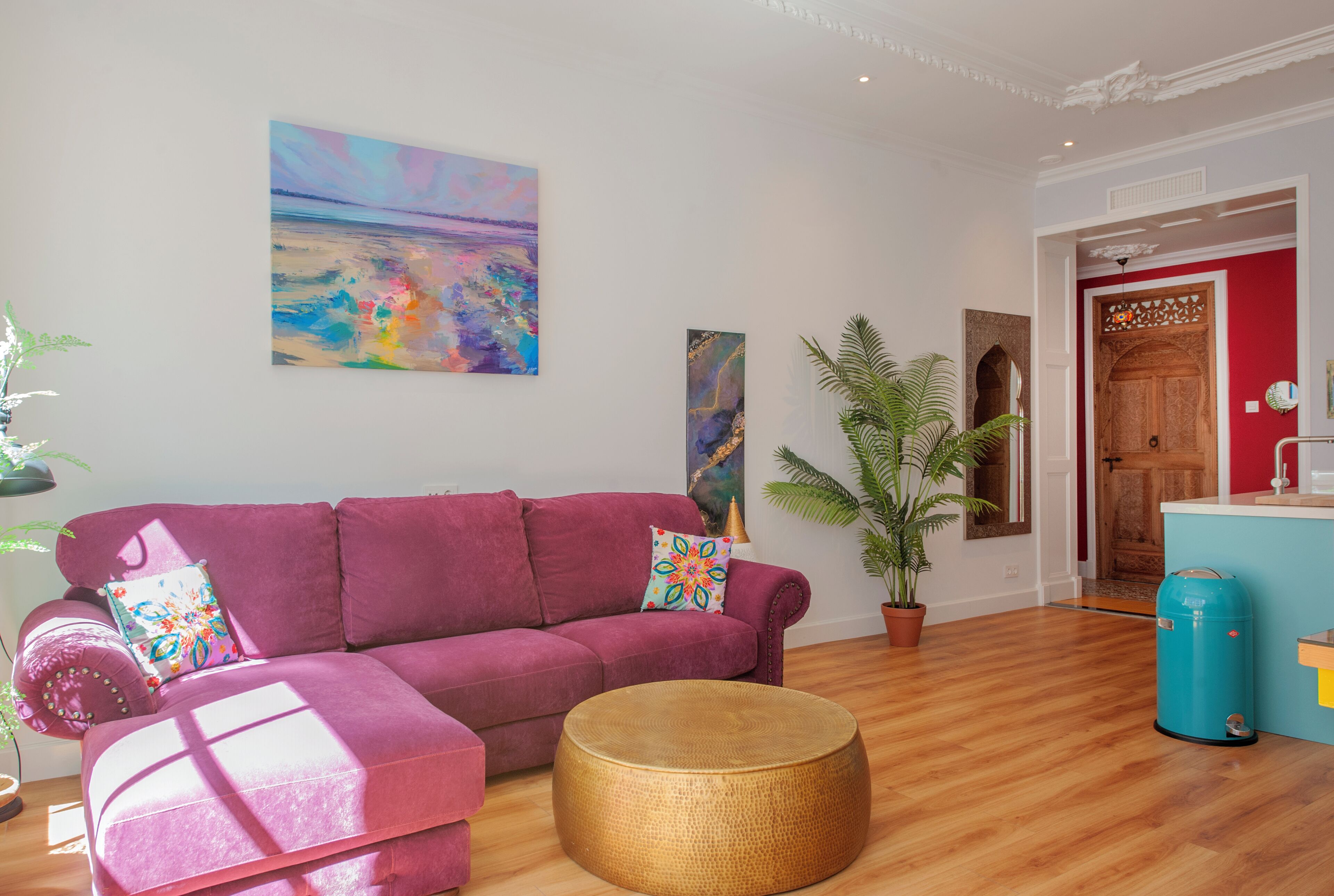 Uma sala de estar moderna com um sofá rosa, um banquinho redondo de madeira e uma grande pintura abstrata na parede.