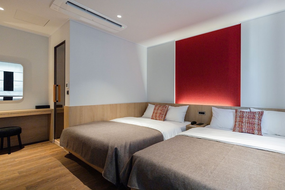 Quarto de hotel com duas camas, uma escrivaninha e uma televisão.