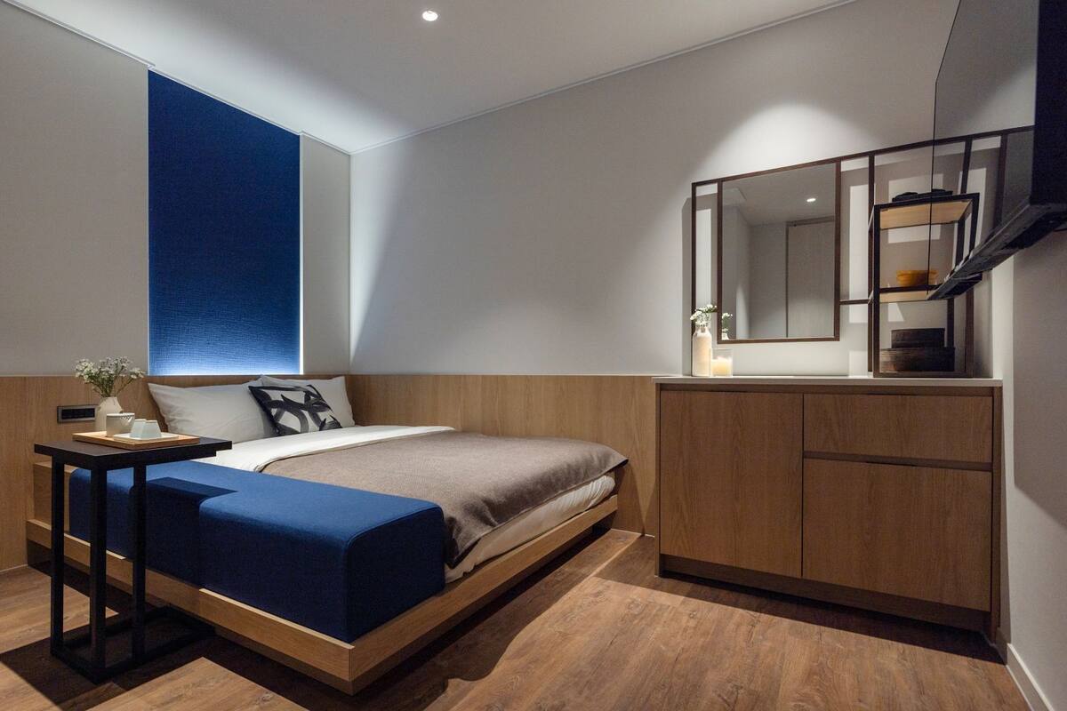 Quarto moderno com cama, mesa de cabeceira e um espelho grande.