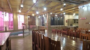 Uma ampla sala de jantar com mesas e cadeiras de madeira, paredes de pedra e luminárias pendentes em estilo lanterna.