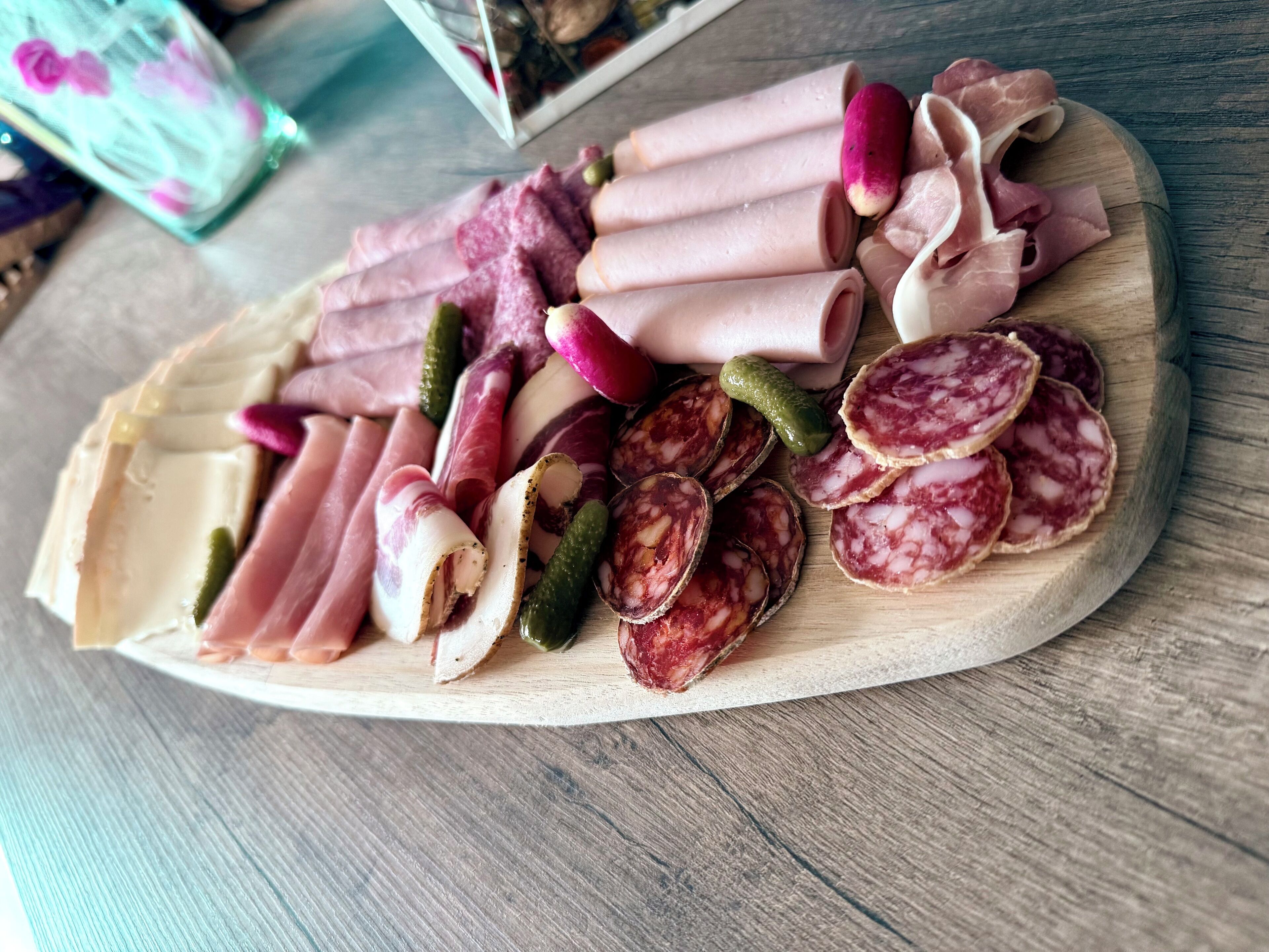 Tábua de madeira com diversos tipos de embutidos e queijos, incluindo salame, presunto e uma seleção de picles.