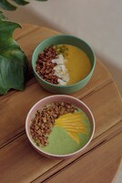 Dois copos de smoothie verde com coberturas sobre uma mesa de madeira.