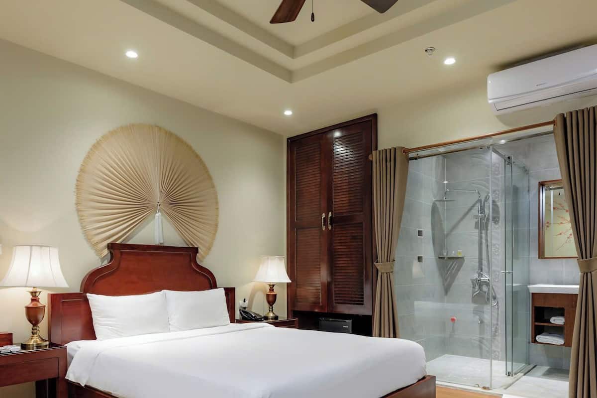 Quarto de hotel com cama grande, ventilador de teto, box de chuveiro em vidro e ar condicionado.