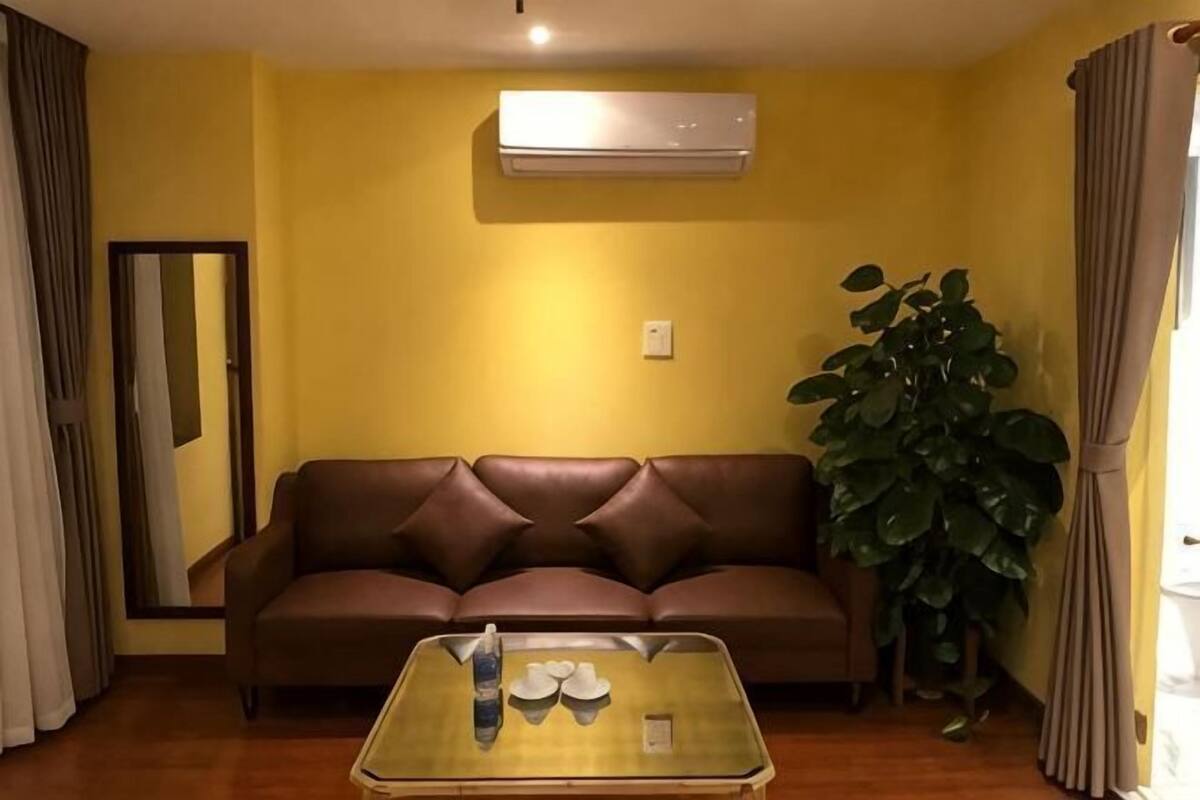 Uma sala de estar com um sofá marrom, uma mesa de centro de vidro e uma grande planta verde.