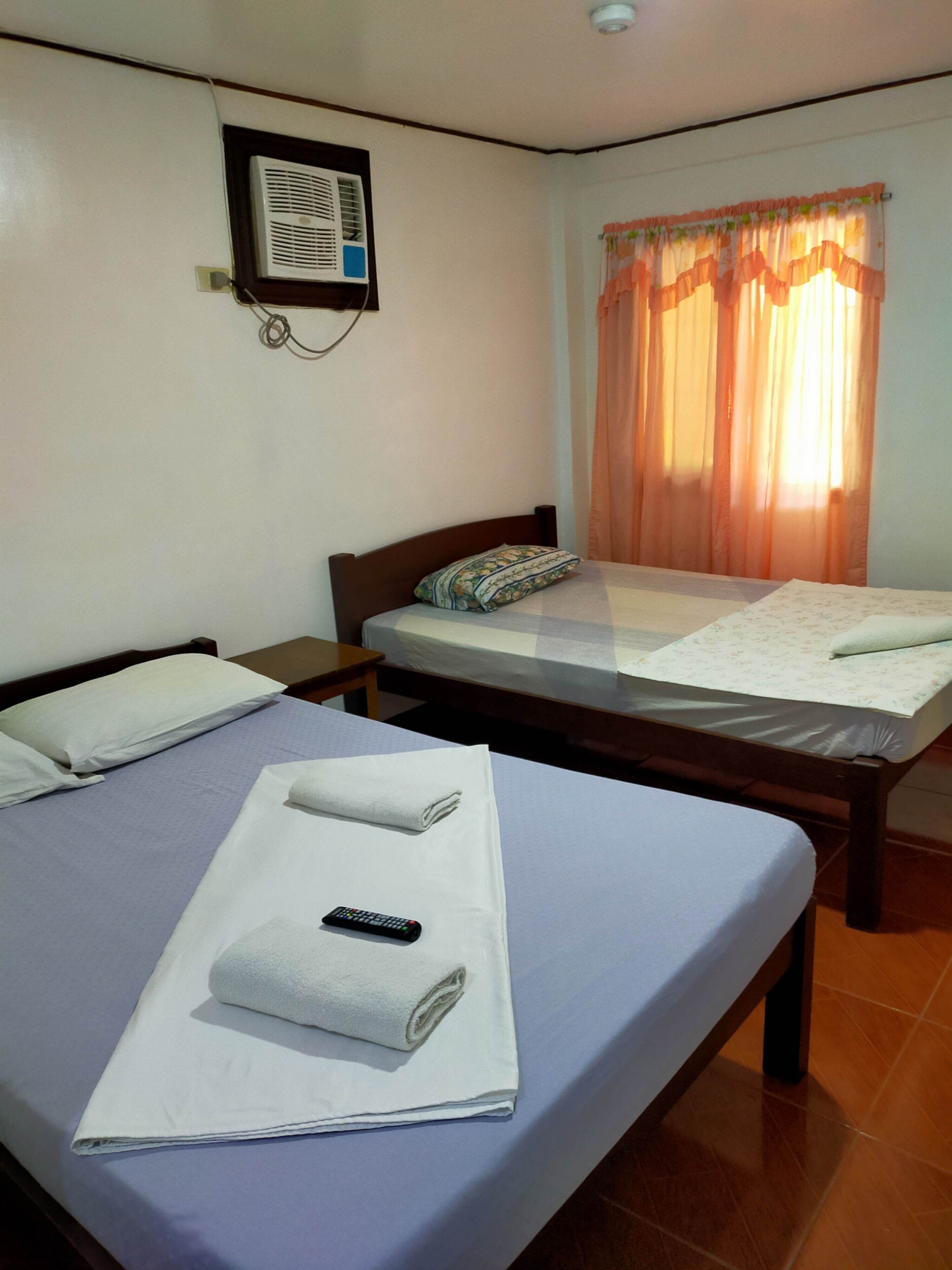 Quarto de hotel com duas camas, uma janela com cortinas, um ar condicionado fixado na parede e uma pequena mesa.