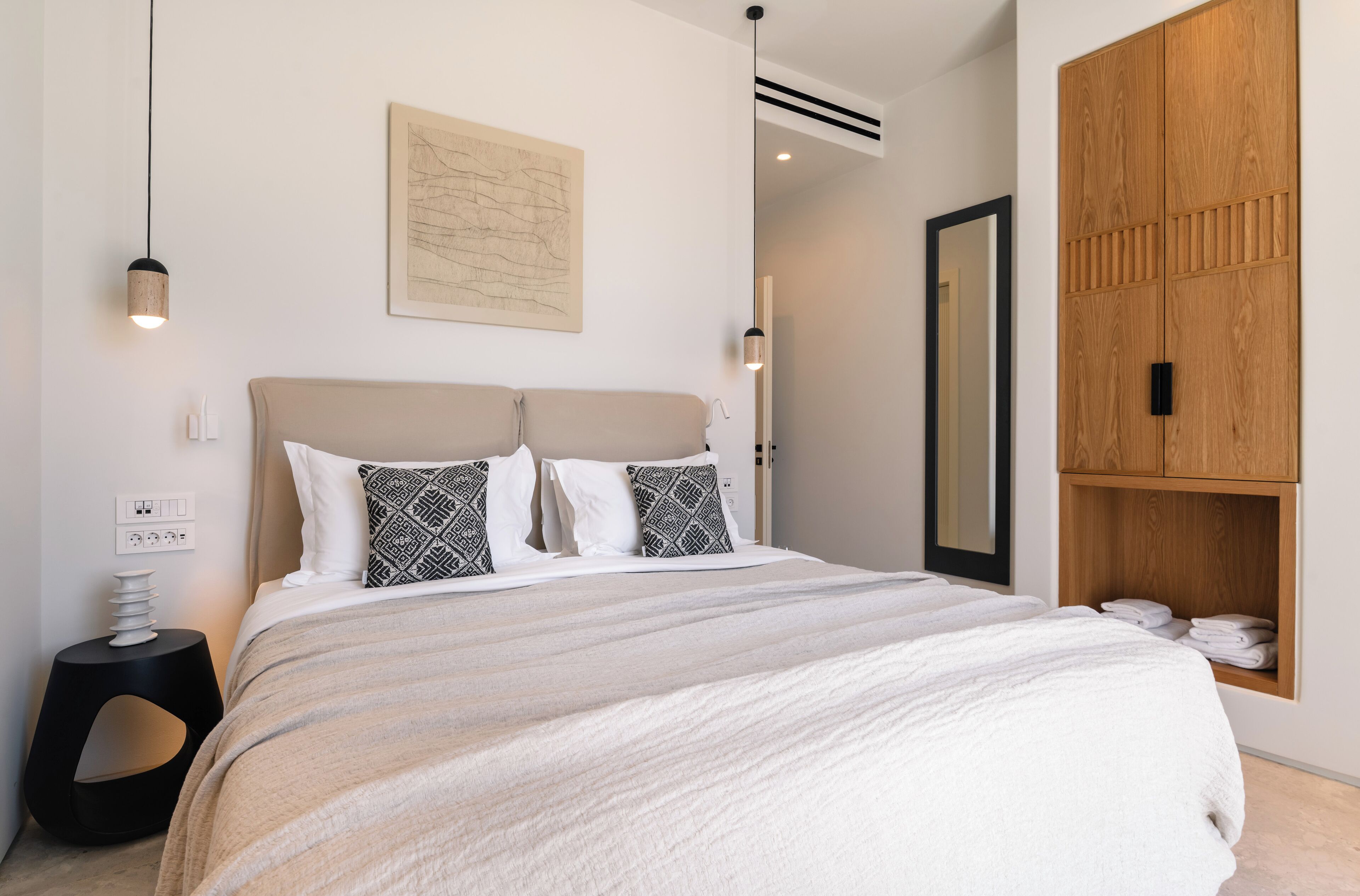 Quarto moderno com uma cama grande, duas mesas de cabeceira, um guarda-roupa de madeira e um espelho fixado na parede.