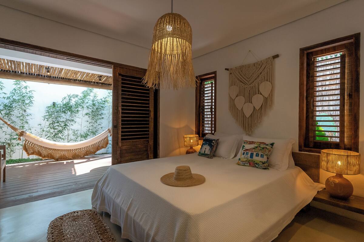Quarto com uma cama grande, rede pendurada e vista para bambus.