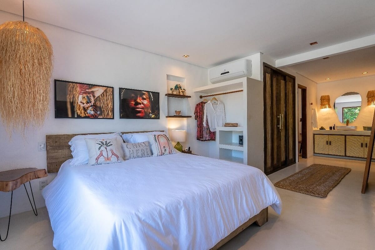 Quarto moderno com cama grande, obra de arte na parede, luminária pendente e roupeiro embutido.