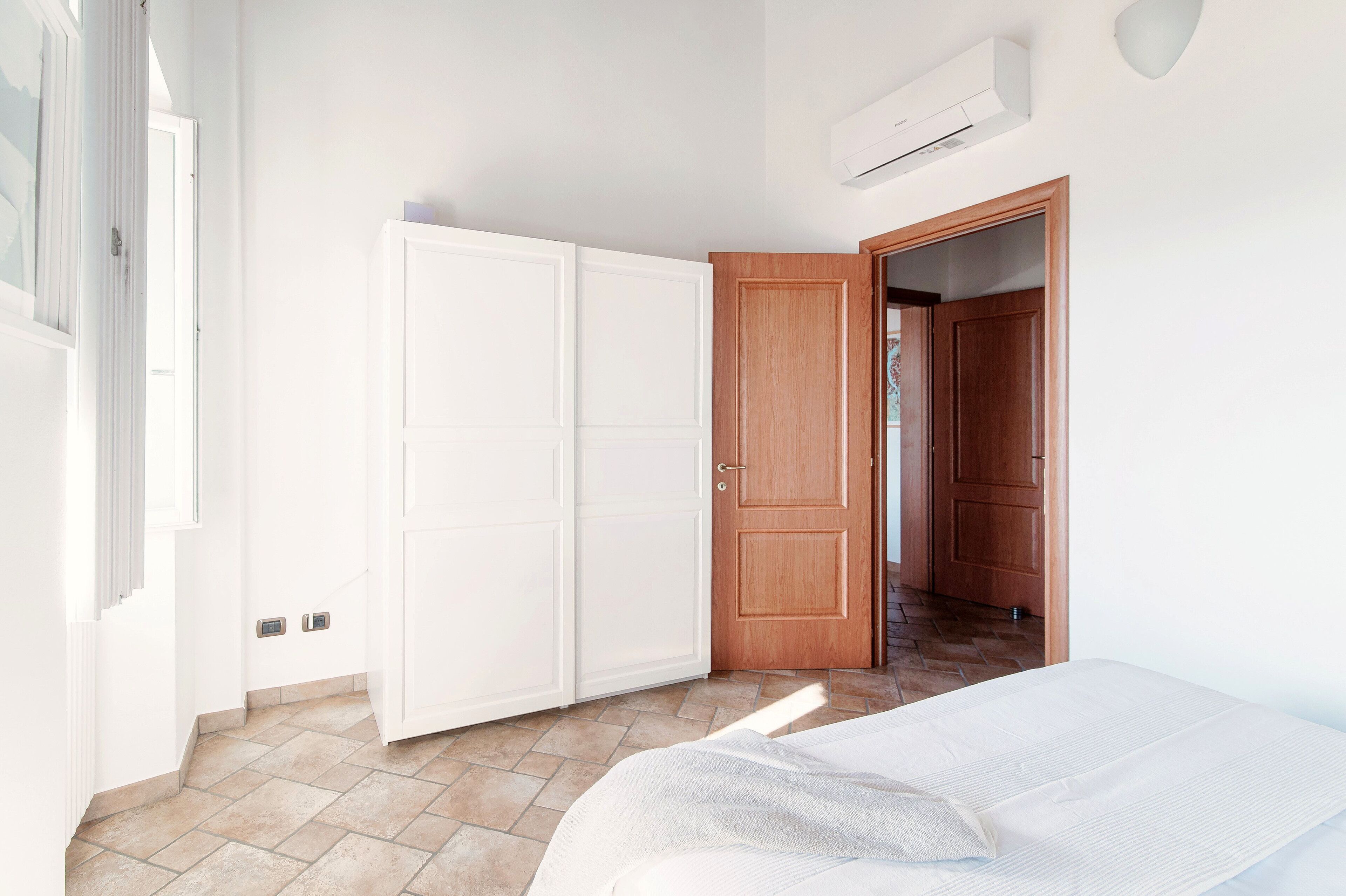 Quarto com cama, guarda-roupa branco, porta de madeira e ar condicionado.
