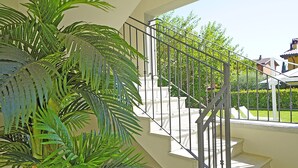 Escada com grades de metal, um vaso de planta e vista para uma casa ao fundo.