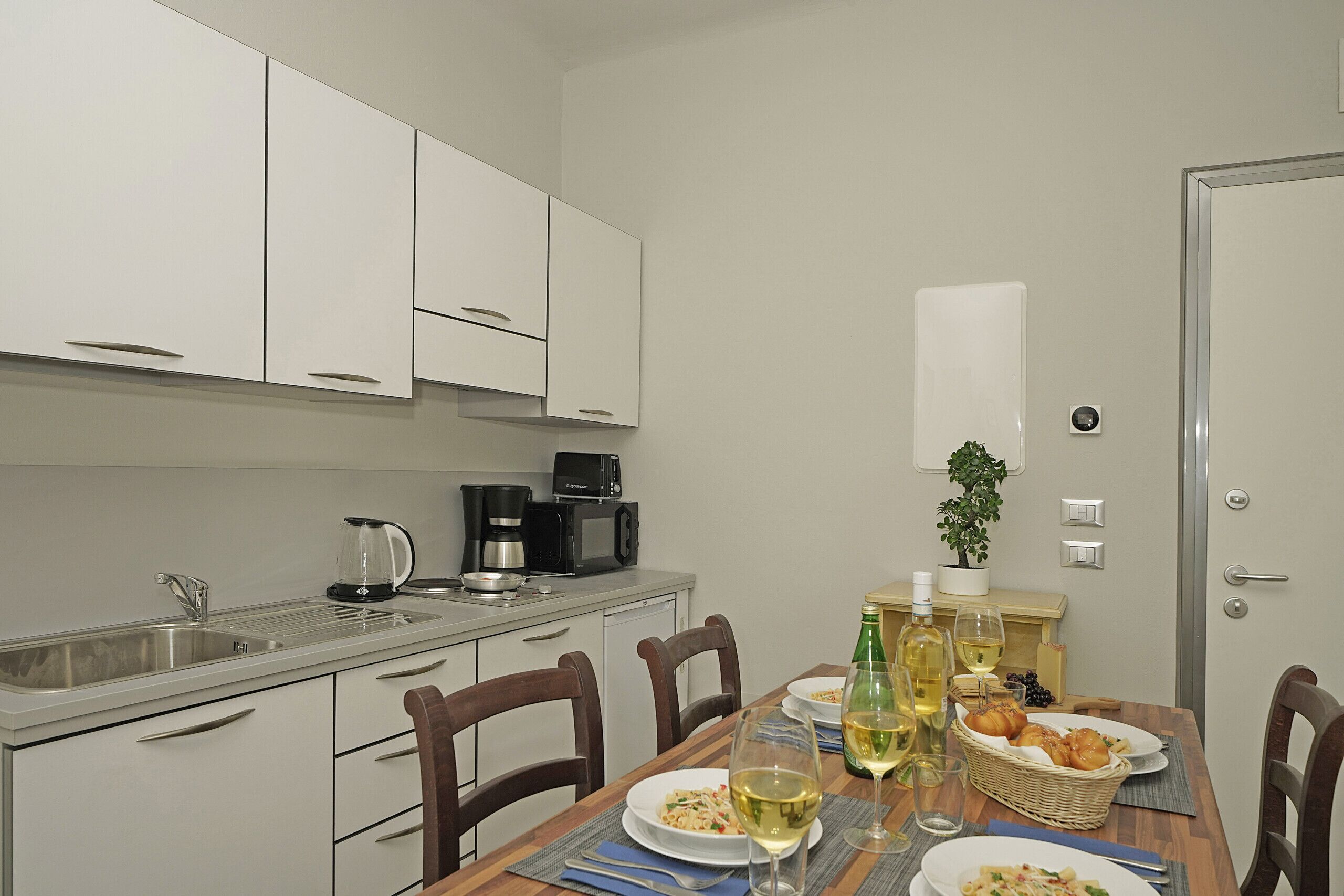Uma cozinha compacta com armários brancos, uma pia e um espaço de jantar com mesa posta para dois.