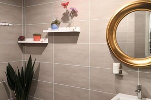 Casa de banho com um espelho grande, uma planta em vaso e duas prateleiras com artigos de higiene pessoal.