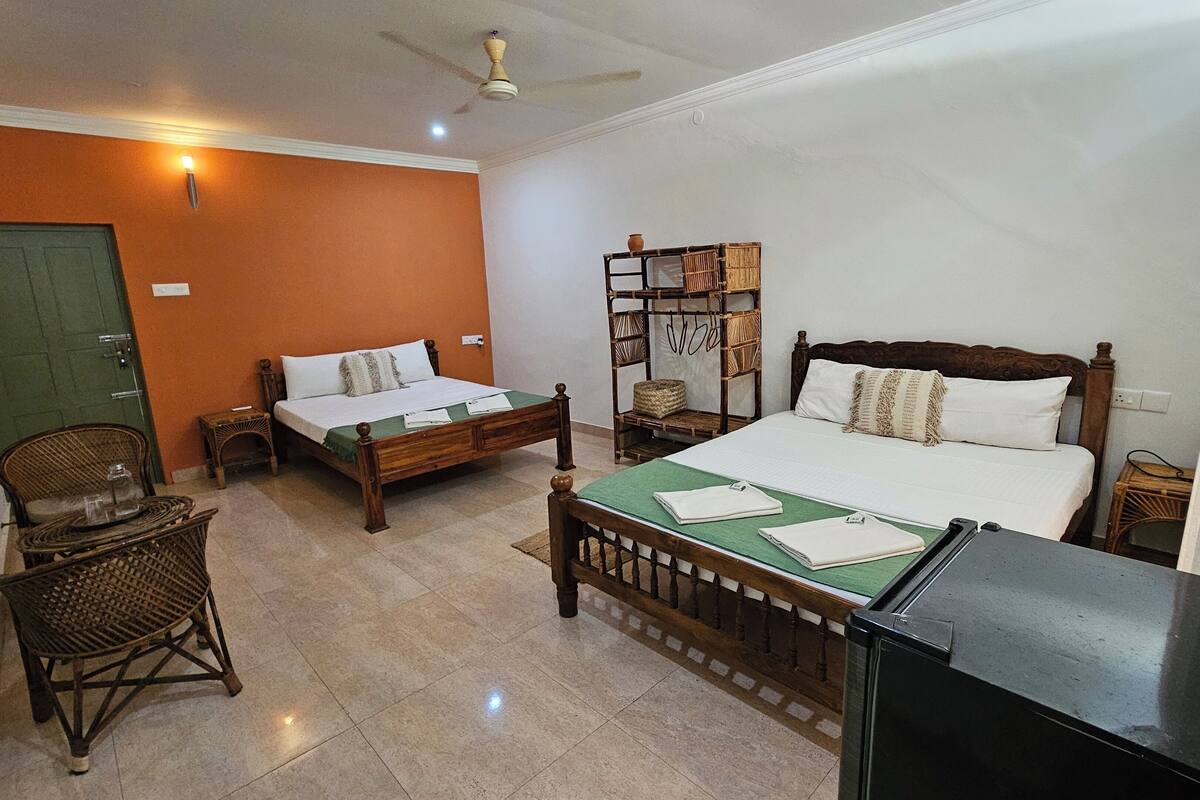 Quarto de hotel com duas camas de madeira, uma cadeira verde, uma mesa pequena e uma televisão.