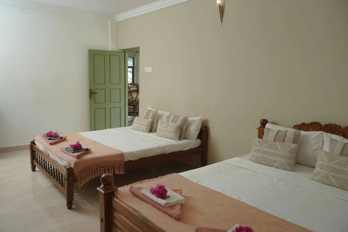 Quarto com duas camas, um banco e uma porta que dá para outro espaço.
