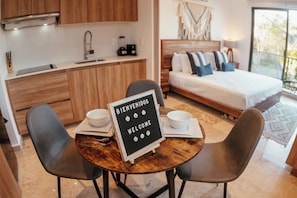 Uma cozinha moderna com armários de madeira, uma pia e uma cafeteira. Há uma área de jantar com mesa e cadeiras, e uma placa que diz "BIENVENIDOS WELCOME".