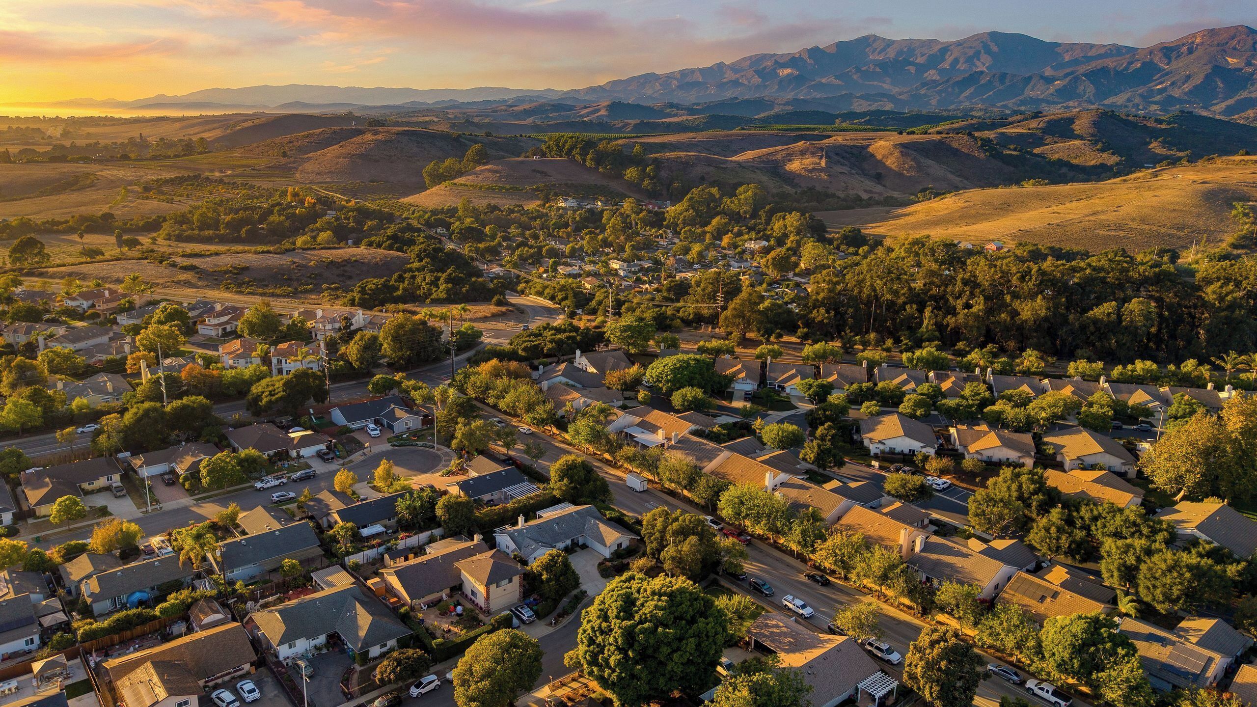 Vista aérea de um bairro residencial com casas, estradas e colinas ao redor.