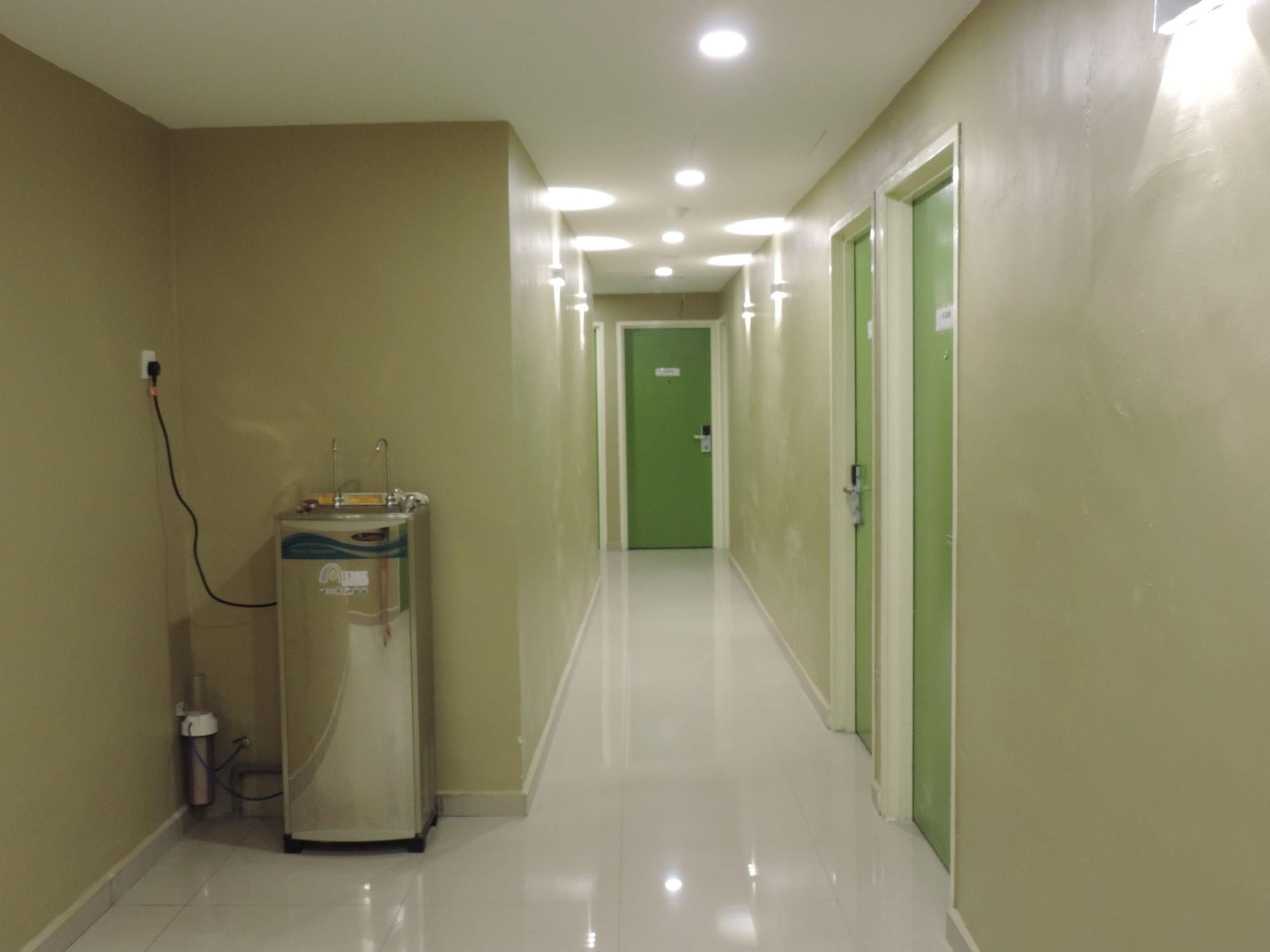 Corredor com bebedouro, porta verde no final e chão limpo.