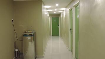 Corredor com bebedouro, porta verde no final e chão limpo.