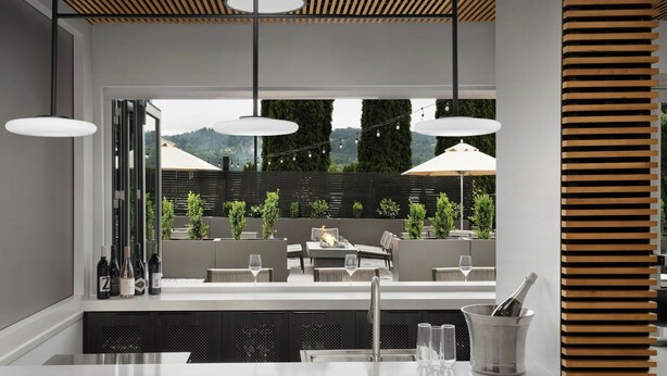 Uma área moderna para refeições ao ar livre, com balcão de bar, assentos e vista para uma paisagem montanhosa.