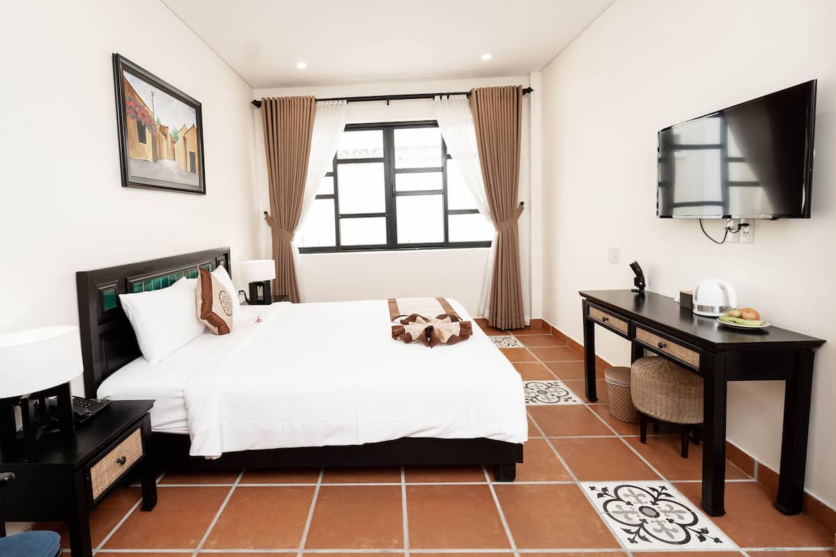 Quarto de hotel com cama, escrivaninha, televisão e janela com cortinas.