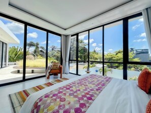 Quarto moderno com uma cama grande, vista para o exterior e um pequeno espaço de estar.