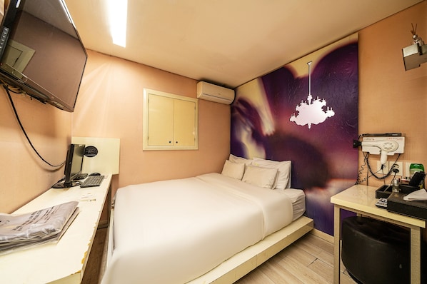 Quarto de hotel com cama, escrivaninha com computador, televisão e ar condicionado fixado na parede.