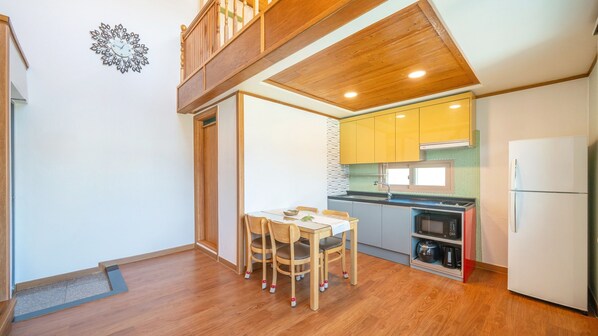 Cozinha compacta com piso de madeira, mesa de jantar com cadeiras, micro-ondas embutido e geladeira.