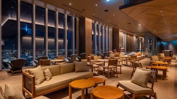 Um lounge moderno com vista para a cidade, com sofás, cadeiras e mesas dispostas para convívio.