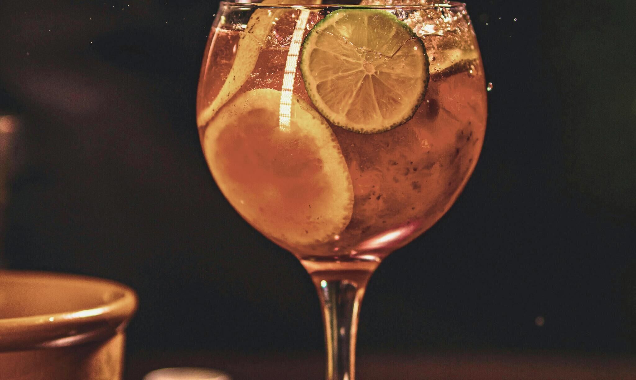 Um copo com uma fatia de limão e um líquido escuro, possivelmente um coquetel, em um bar.